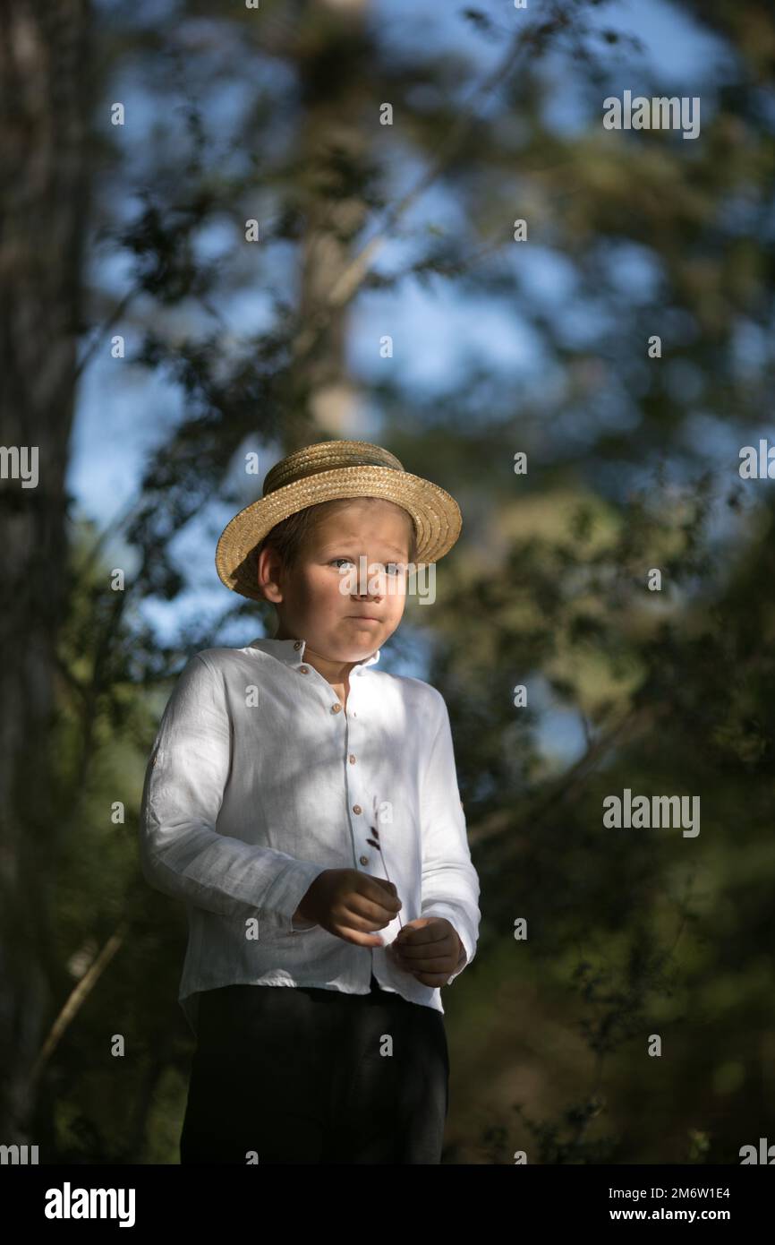 Small farm boy, smiling and looking at the camera, stands in forest ...