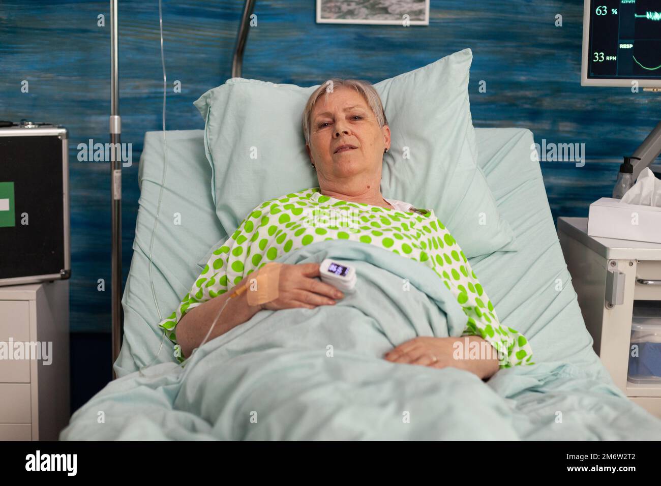 Elderly woman lying in hospital bed while vital signs and blood oxygen ...