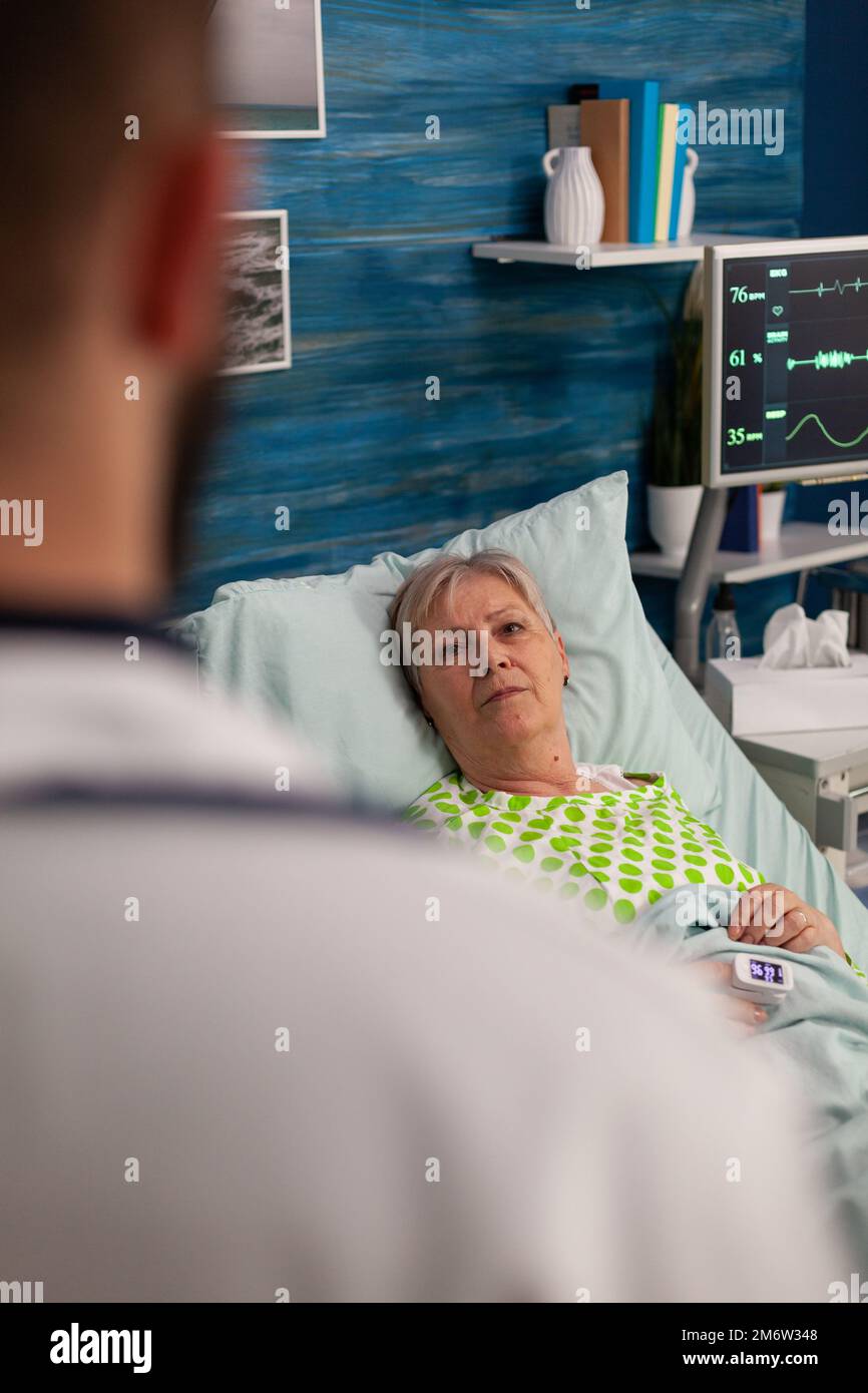 Retired woman lying in hospital bed discussing medical treatment with ...