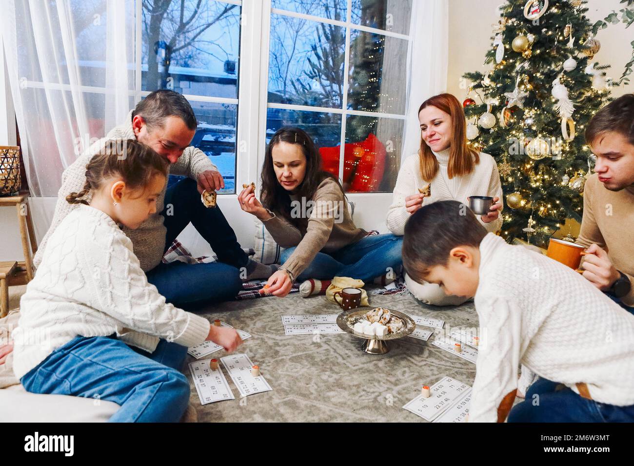 Big family gathering near Xmas tree playing lotto board game at home ...