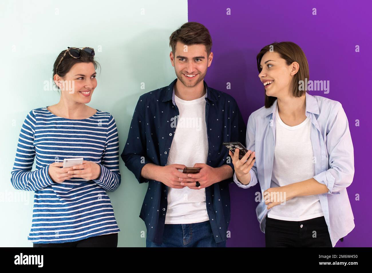 Diverse teenagers using mobile devices while posing for a studio photo ...
