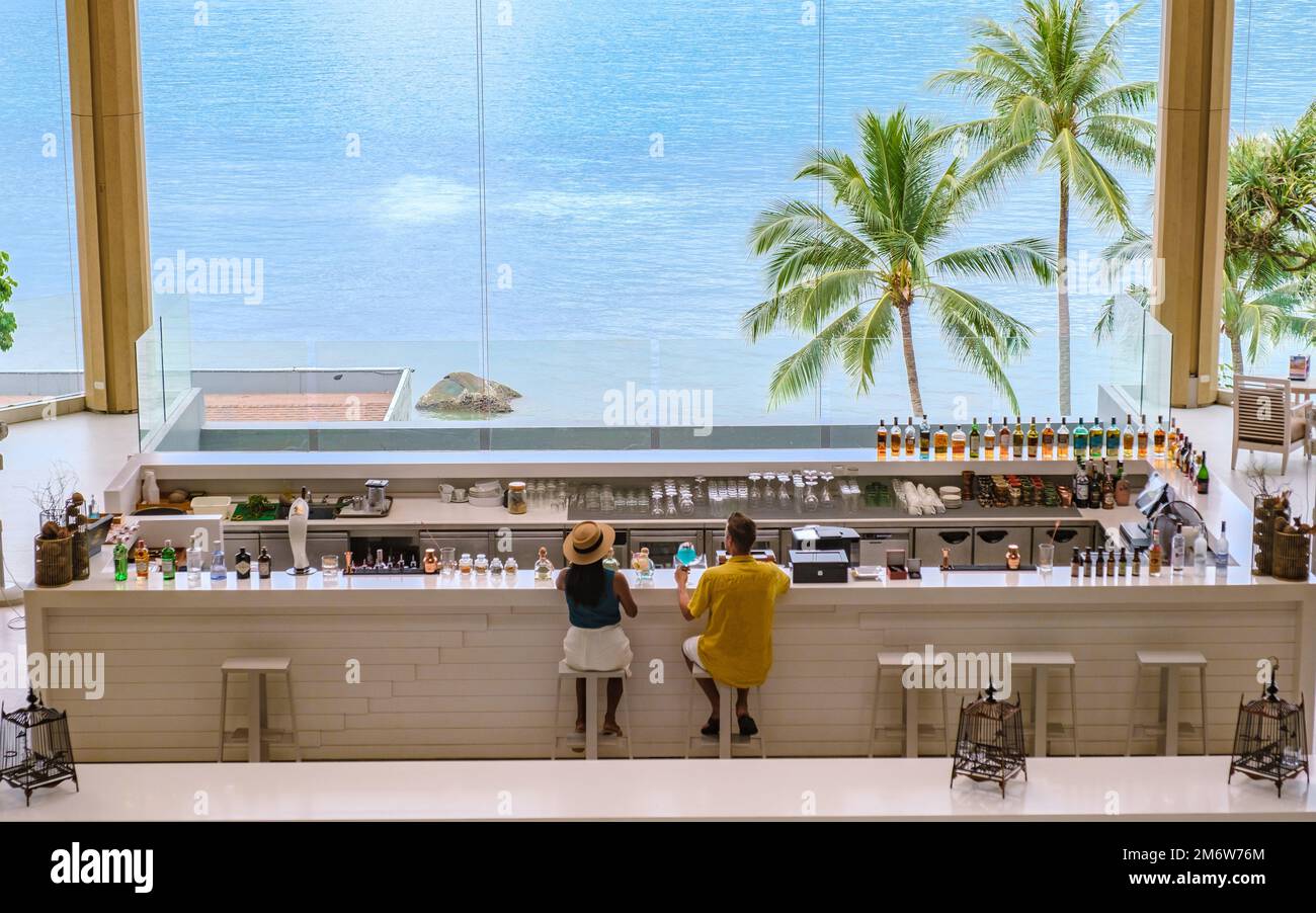 Couple drinking cocktails at a bar during vacation looking out over the ...