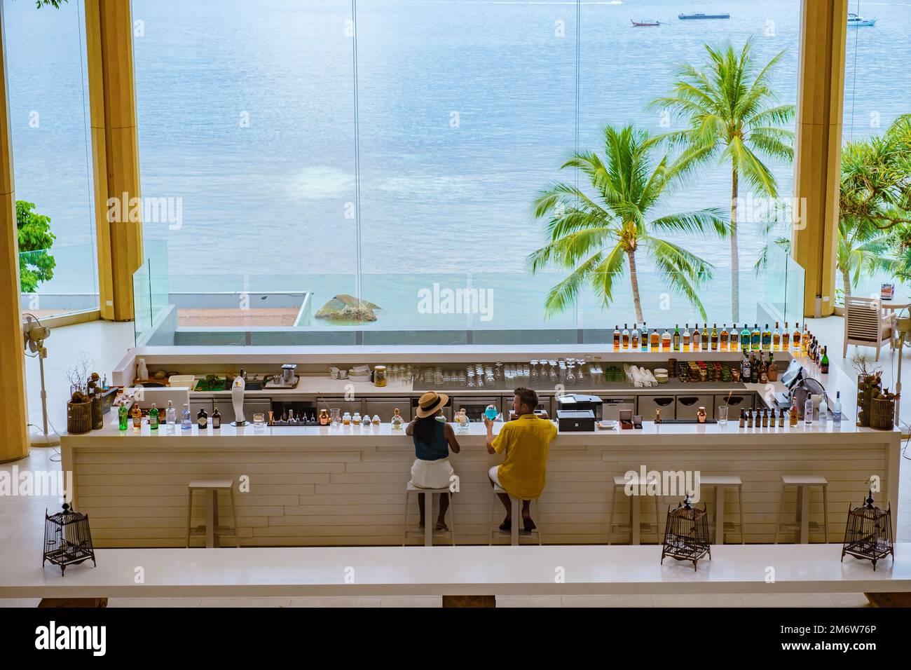 Couple drinking cocktails at a bar during vacation looking out over the ...