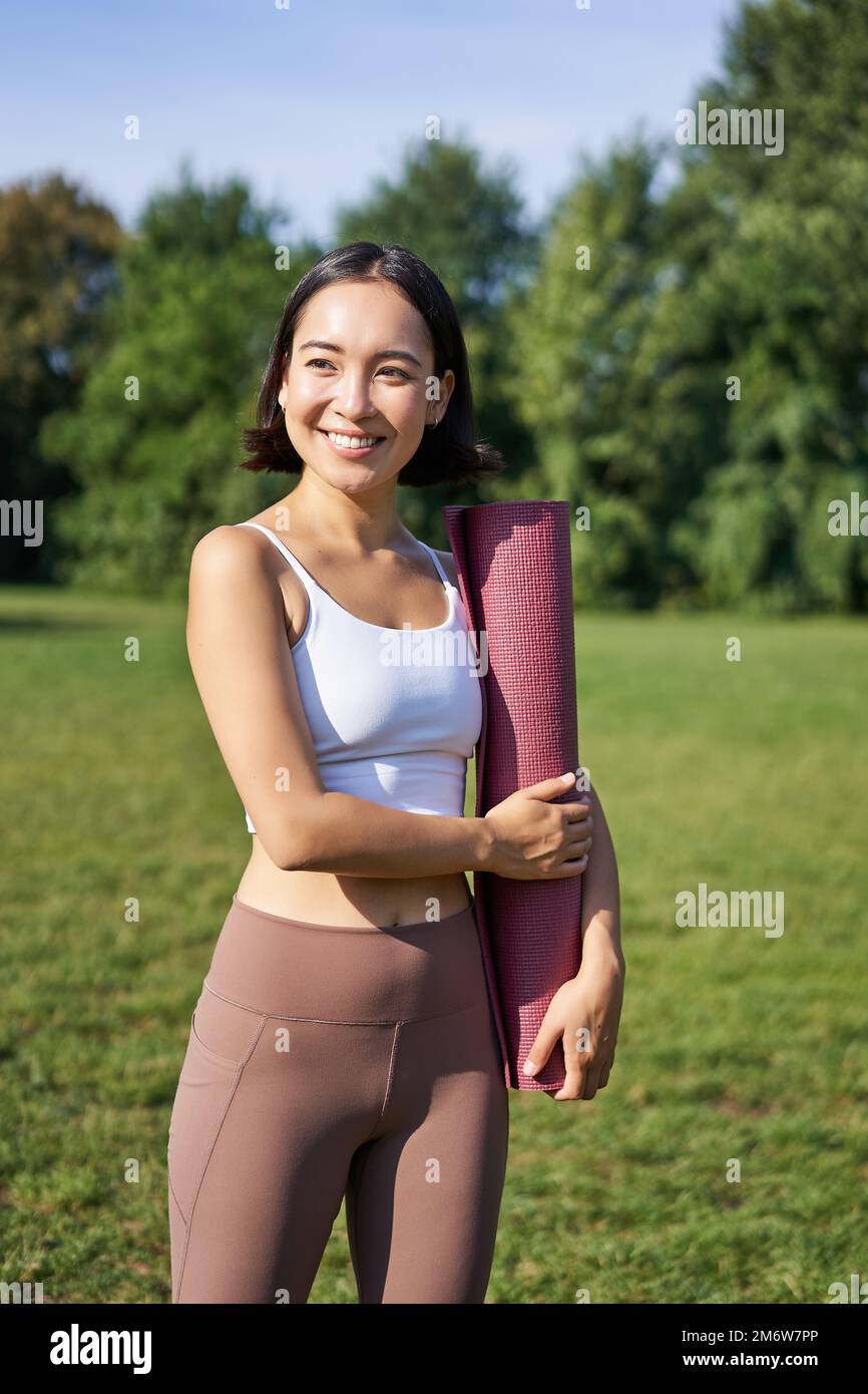 Vertical portrait of young asian fitness girl walks with rubber mat for ...