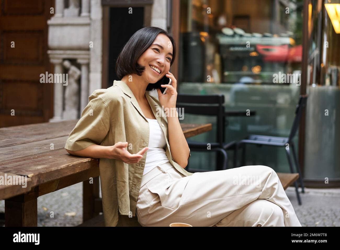 Young woman having conversation on mobile phone, sitting outdoors and ...