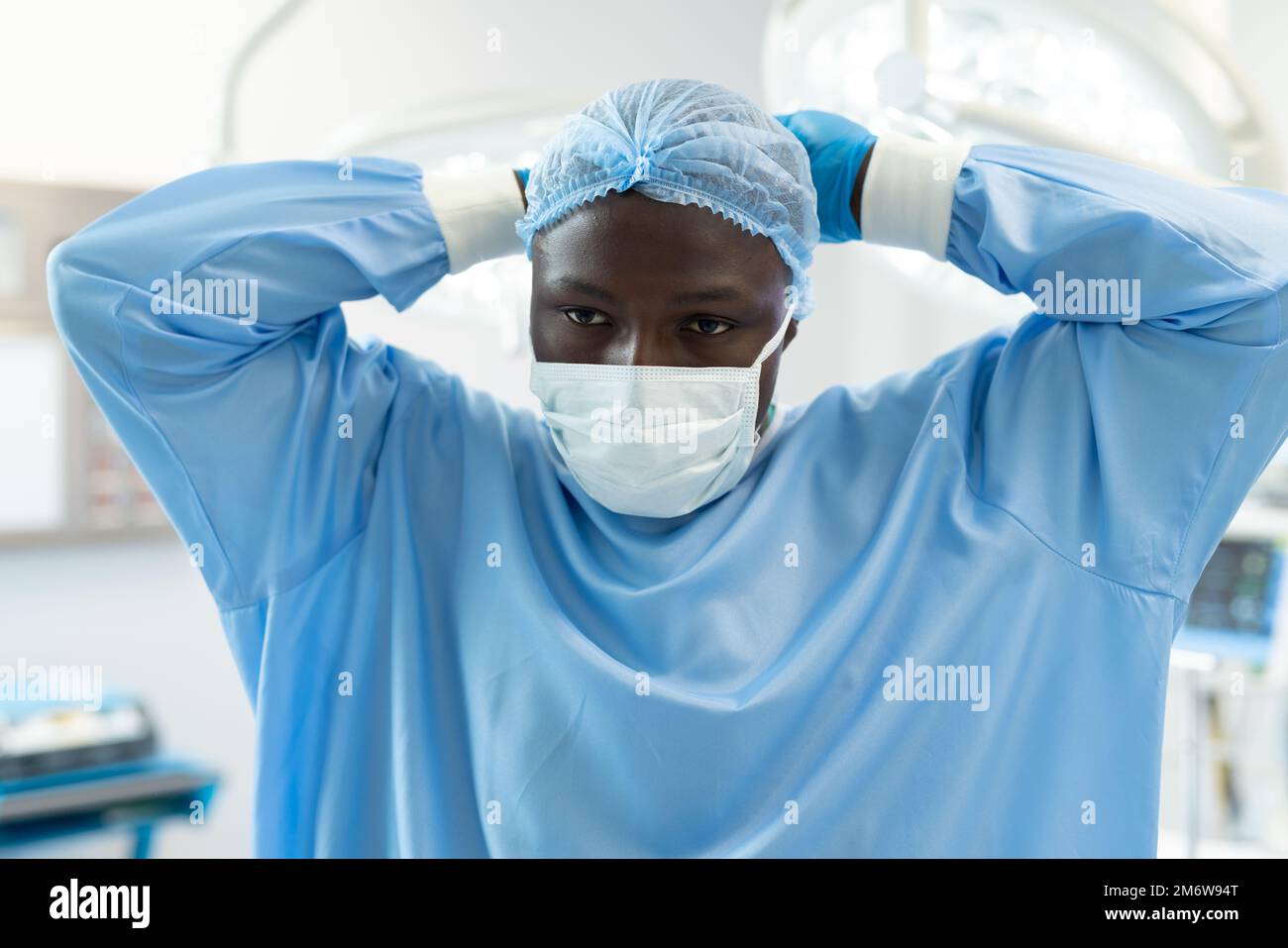 African american male surgeon in surgical gown and cap tying on mask in ...