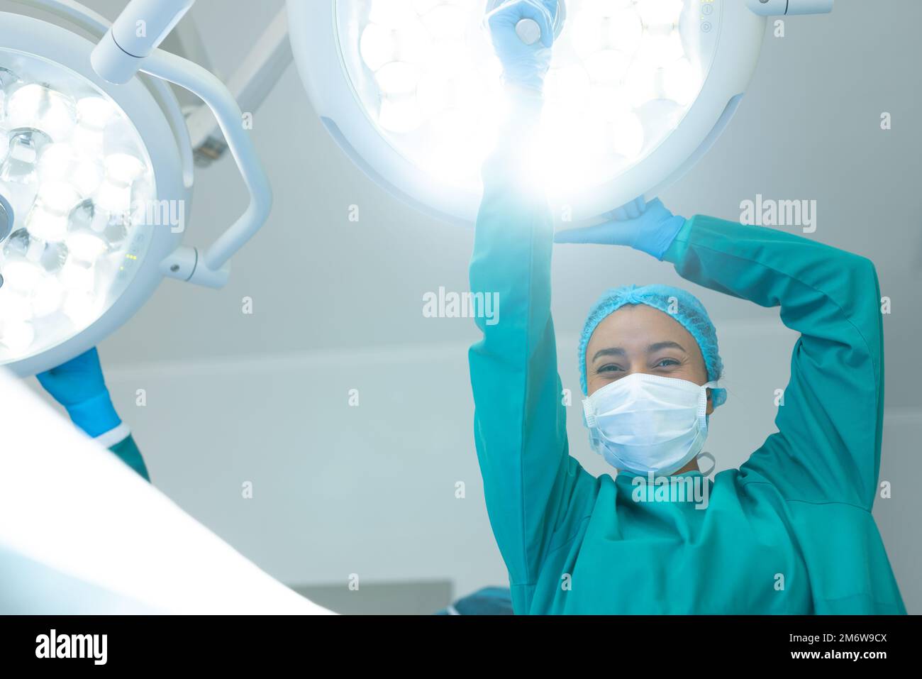 Smiling biracial female surgeon adjusting lights in operating theatre ...