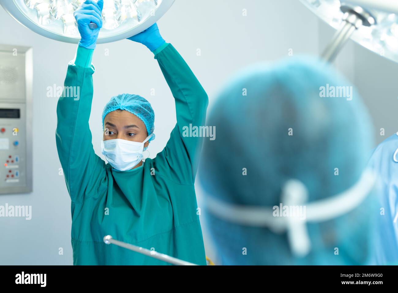 Biracial female surgeon and colleague adjusting lights in operating ...