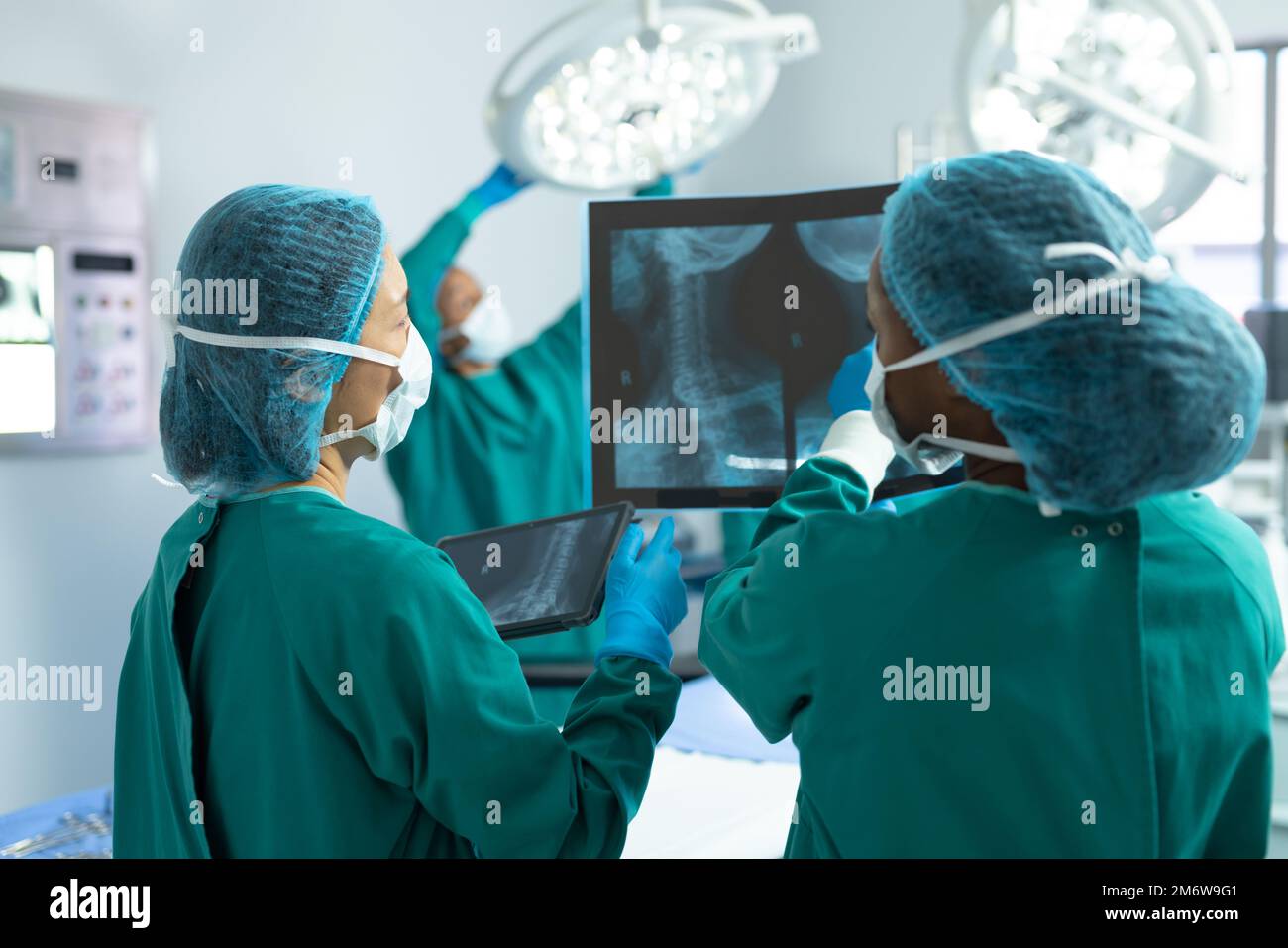 Rear view of two diverse female surgeons discussing x-ray in operating ...