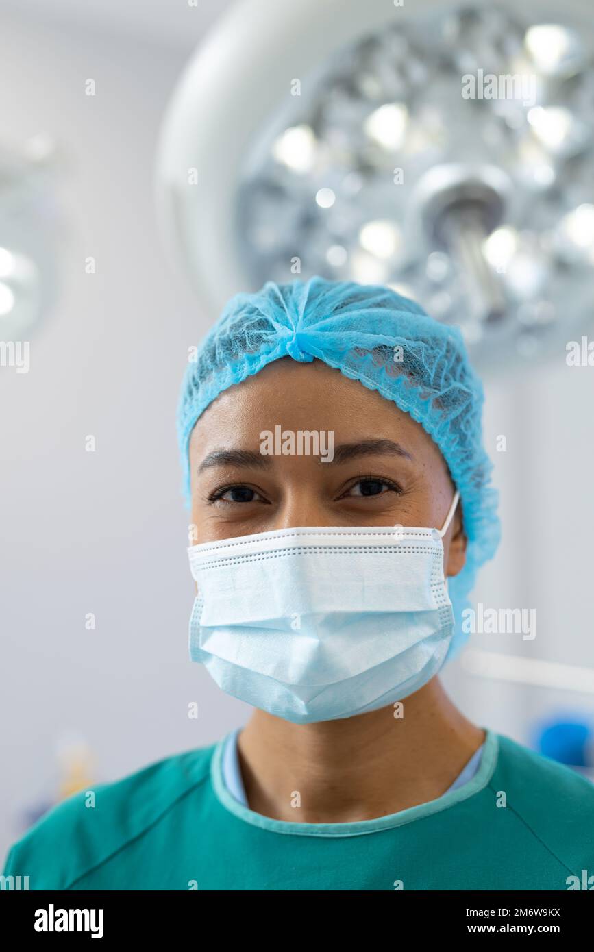 Vertical portrait of smiling biracial female surgeon in surgical mask ...