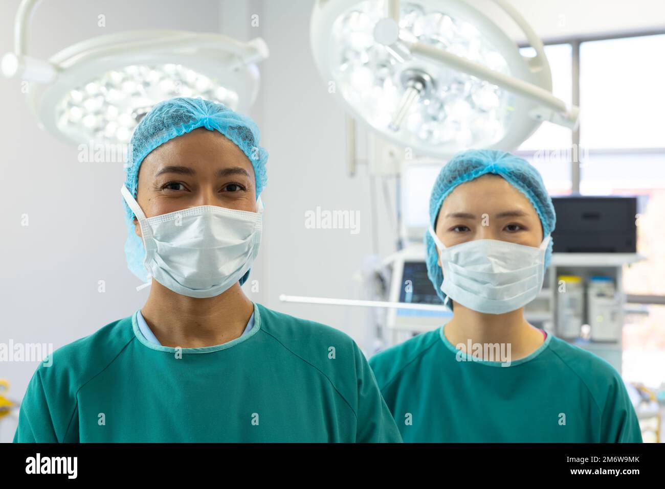 Portrait of two diverse female surgeons in caps and masks smiling in ...