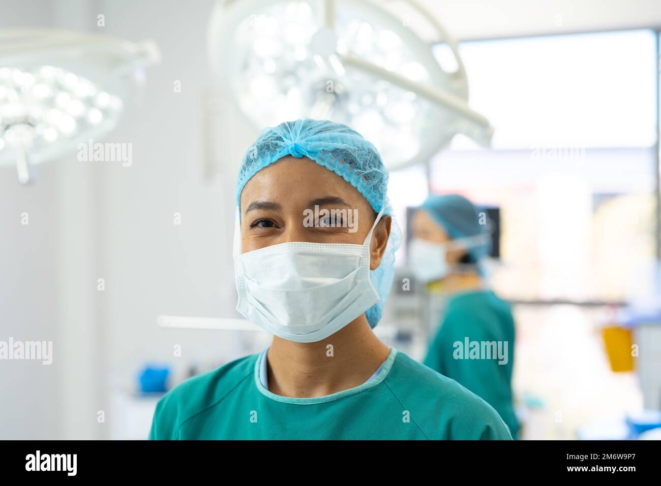 Portrait of smiling biracial female surgeon in mask and cap in ...