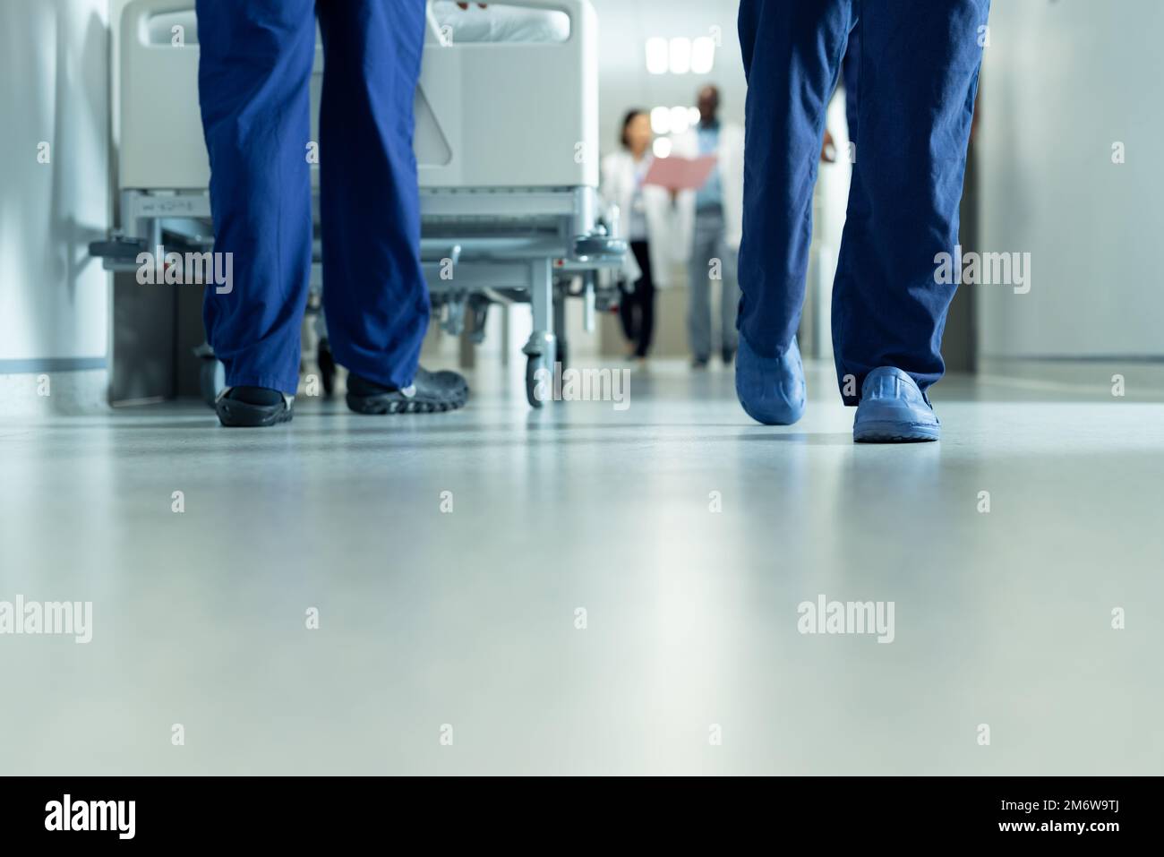 Low section of legs of hospital workers walking and hospital bed in ...