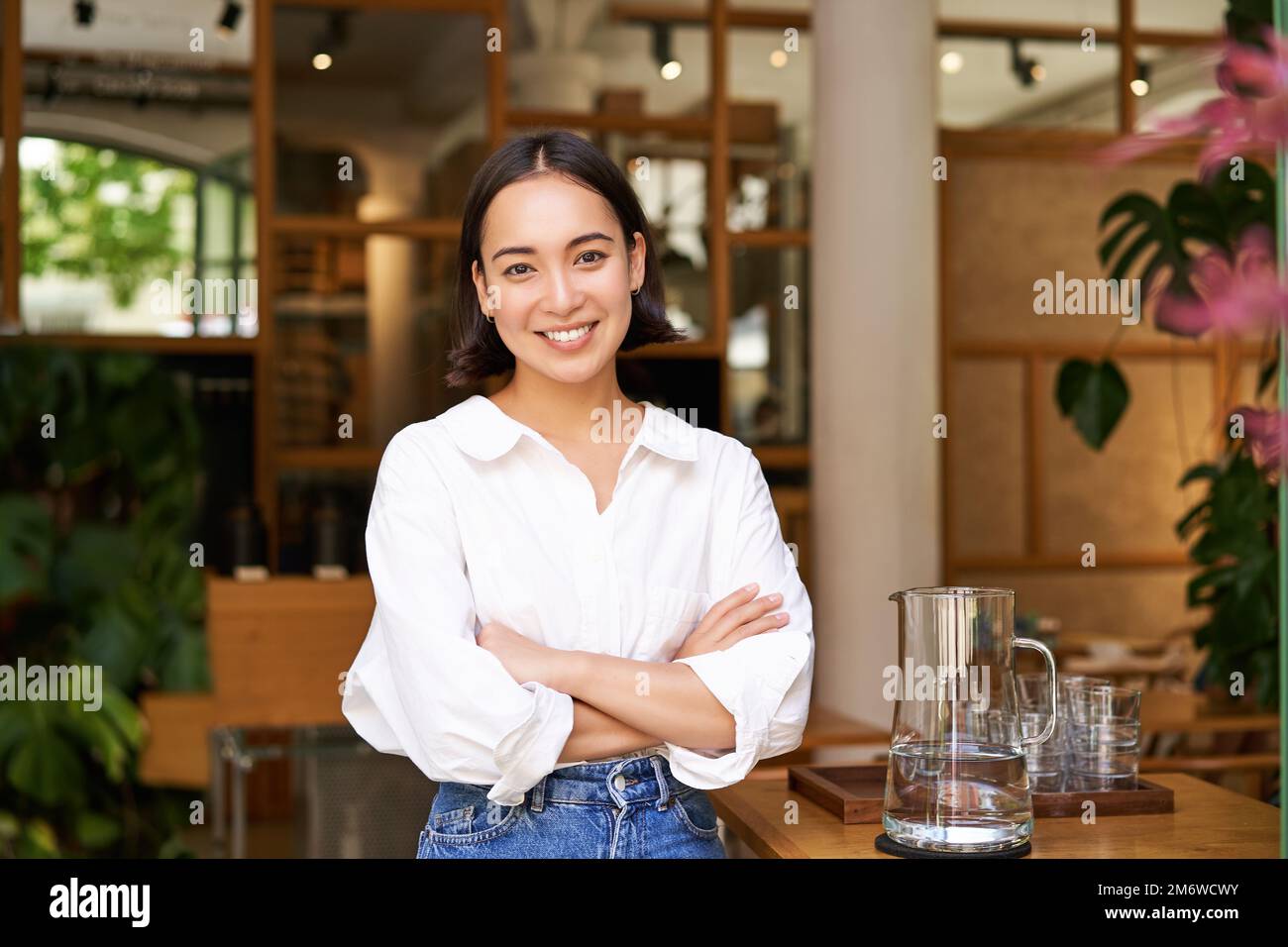 Young asian woman, cafe owner or manager, standing confident with arms ...