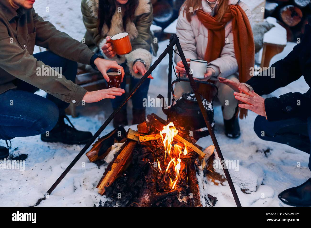 Group of friends gathering around bonfire in backyard, drinking tea and ...