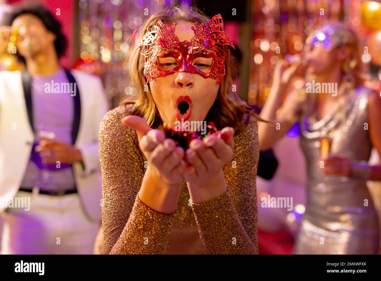 Happy caucasian woman in mask blowing glitter on the dancefloor at a ...