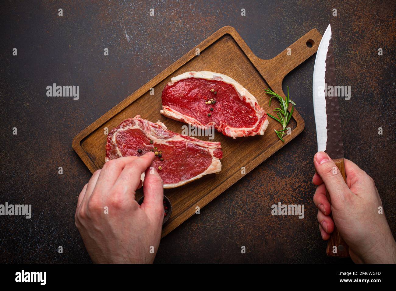 Male's hand holding knife over two raw meat beef steaks top view Stock ...