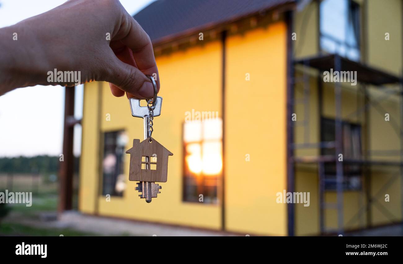 A hand with the keys to a new house on the background of an unfinished ...