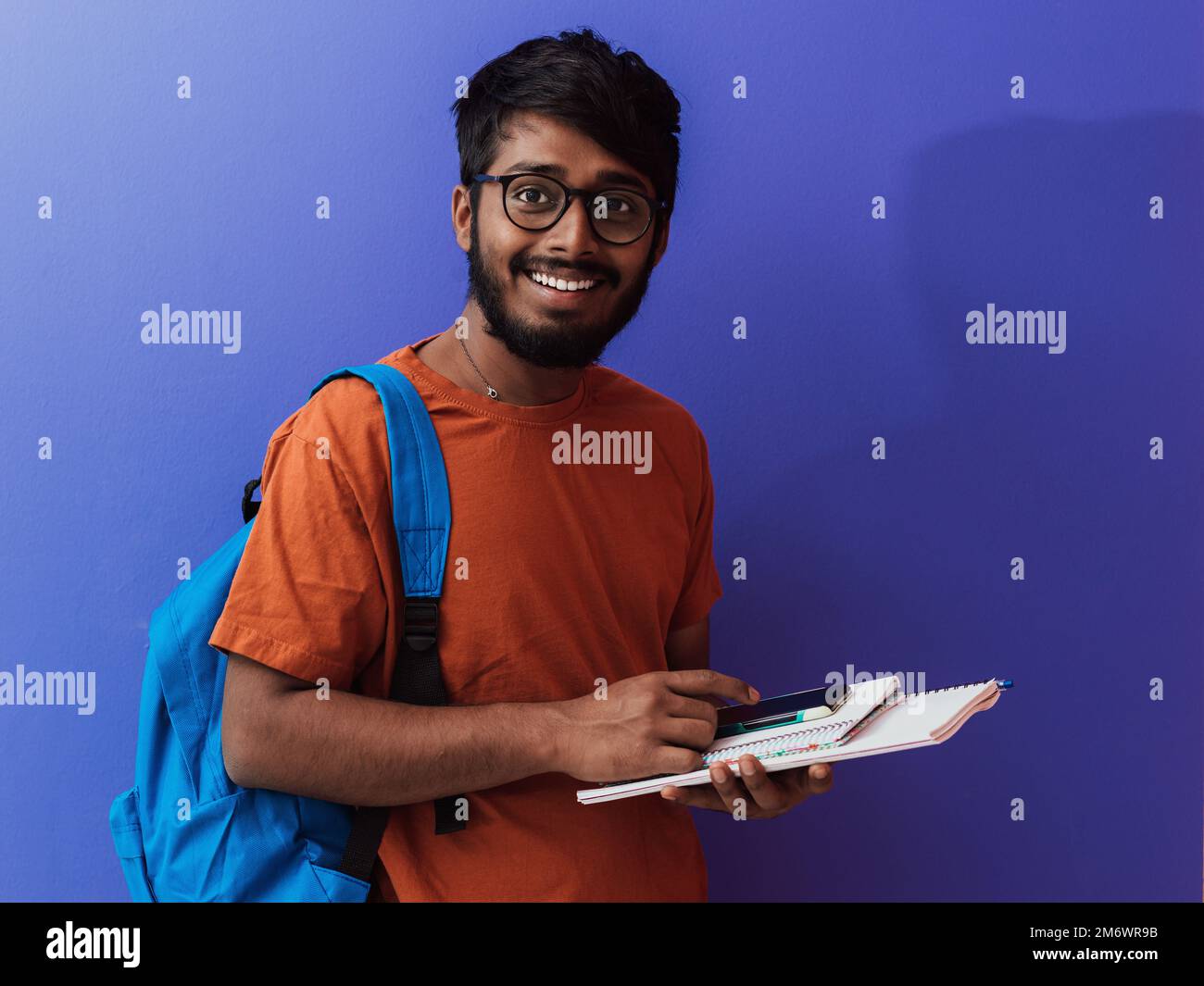 Indian student with blue backpack, glasses and notebook posing on ...