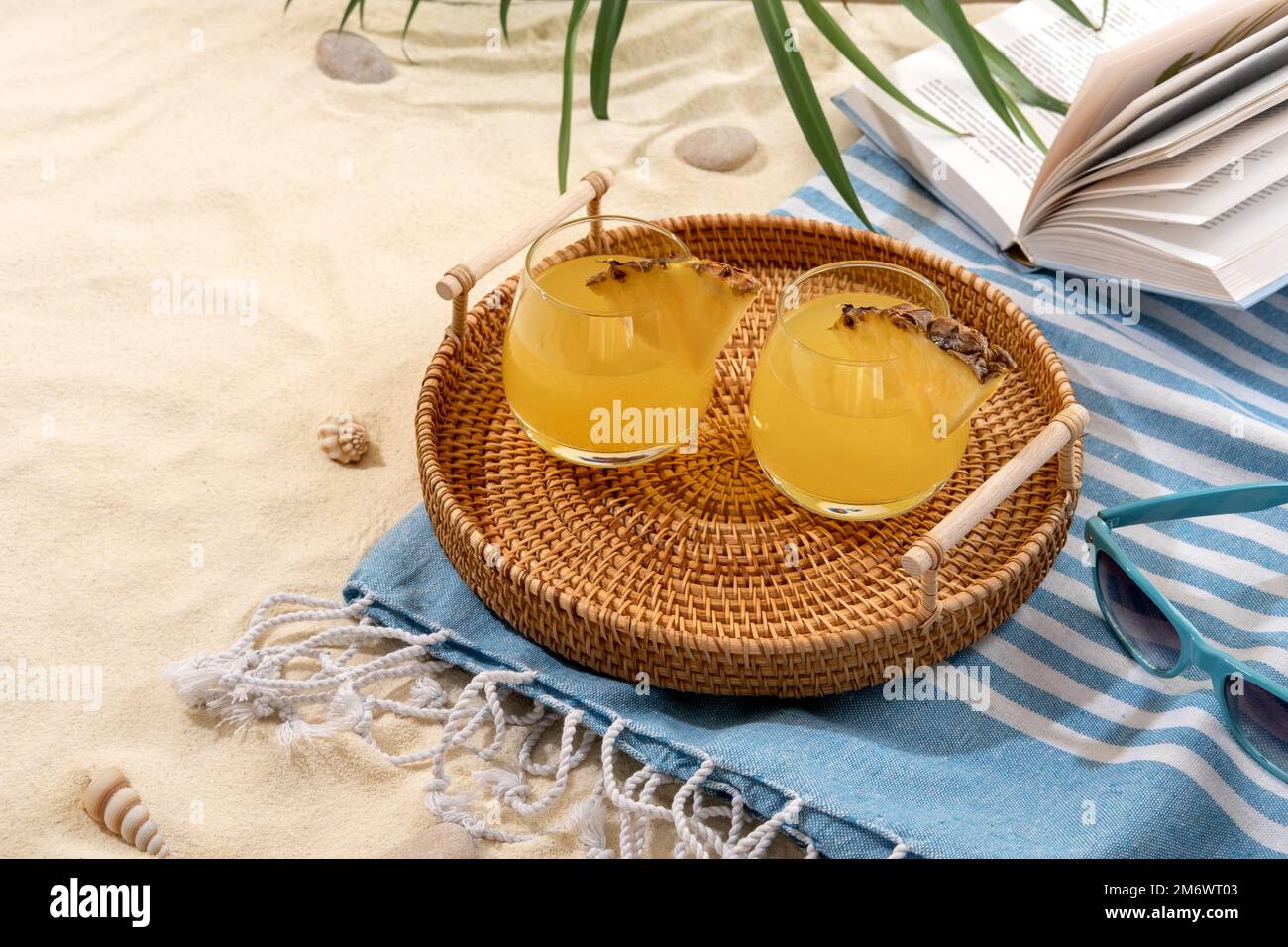Cold pineapple cocktails on a wicker tray on beach with white sand ...