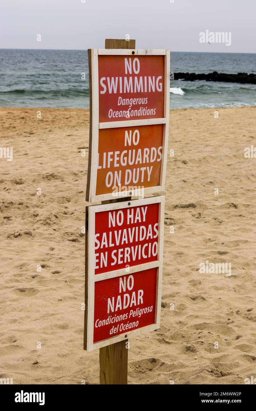 Warning sign on the beach with the ocean and jetty in the background ...