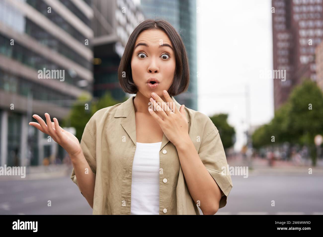 Modern asian girl standing on street with surprised face, looking ...