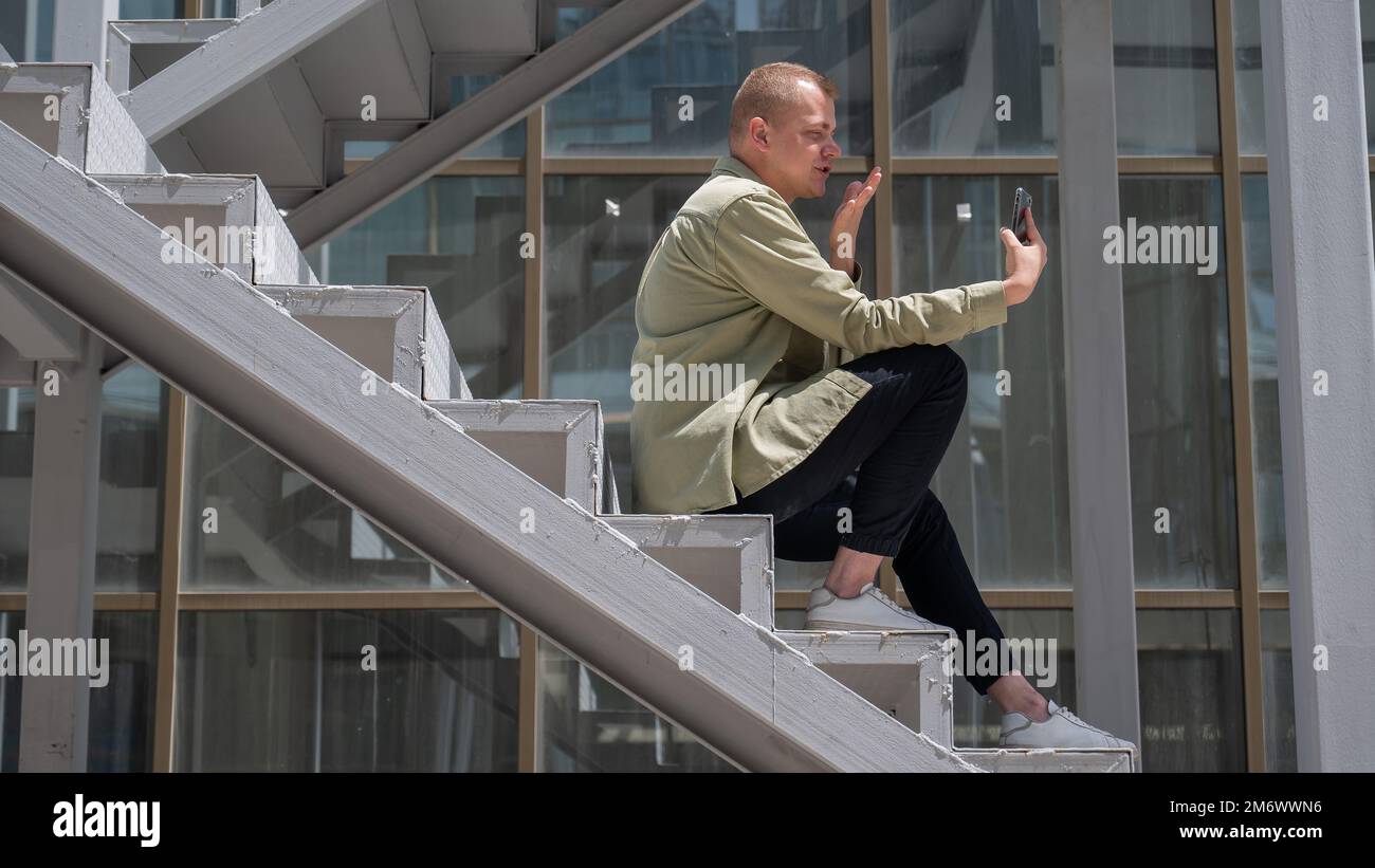 Young man sitting on the stairs and talking sign language via video ...