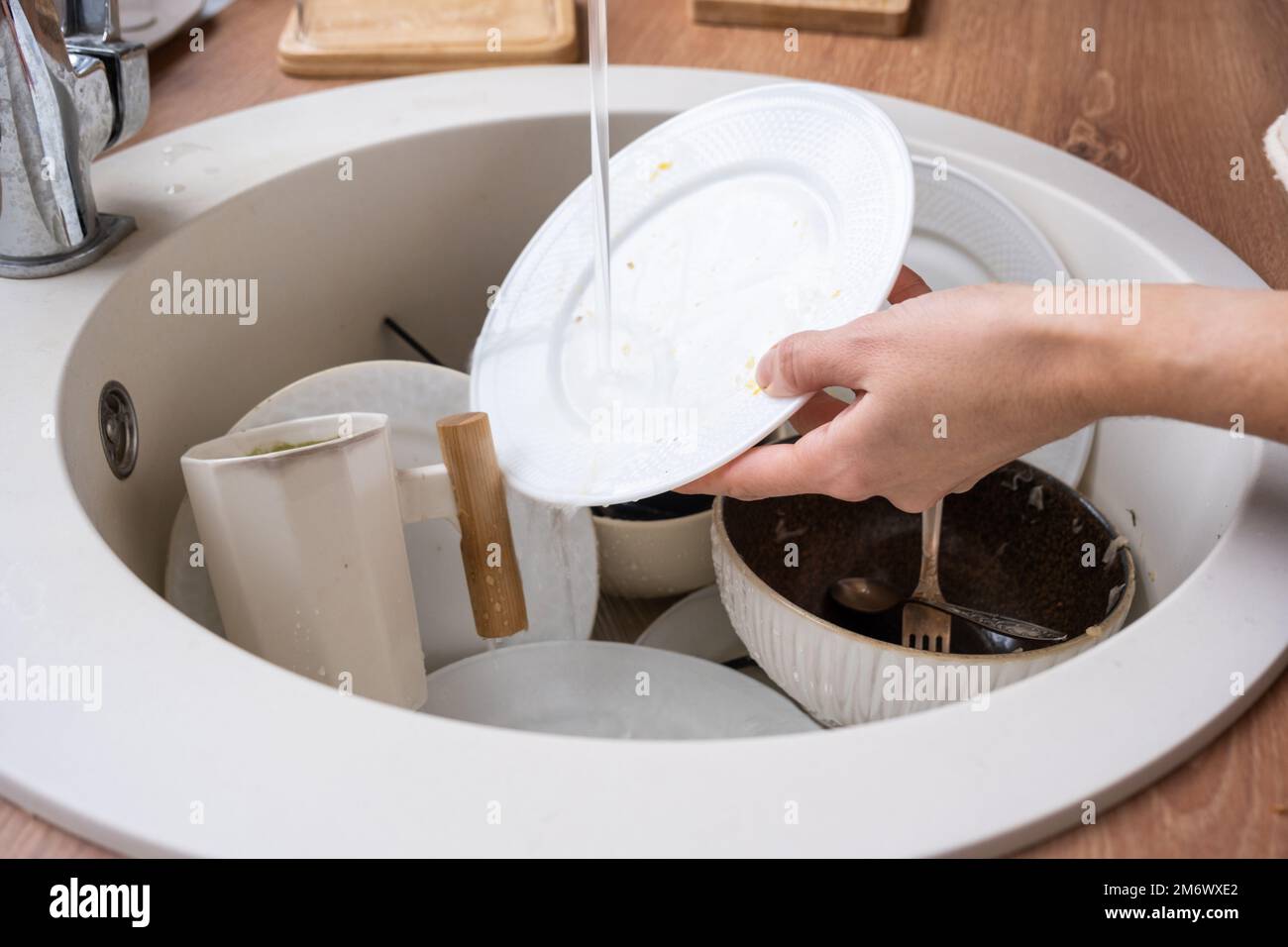 Women's hands wash the plate under the tap water. Dirty dishes in the ...