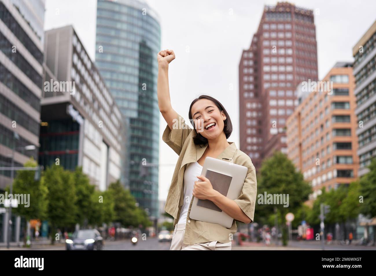 Portrait of happy asian woman stands with tablet near street road ...