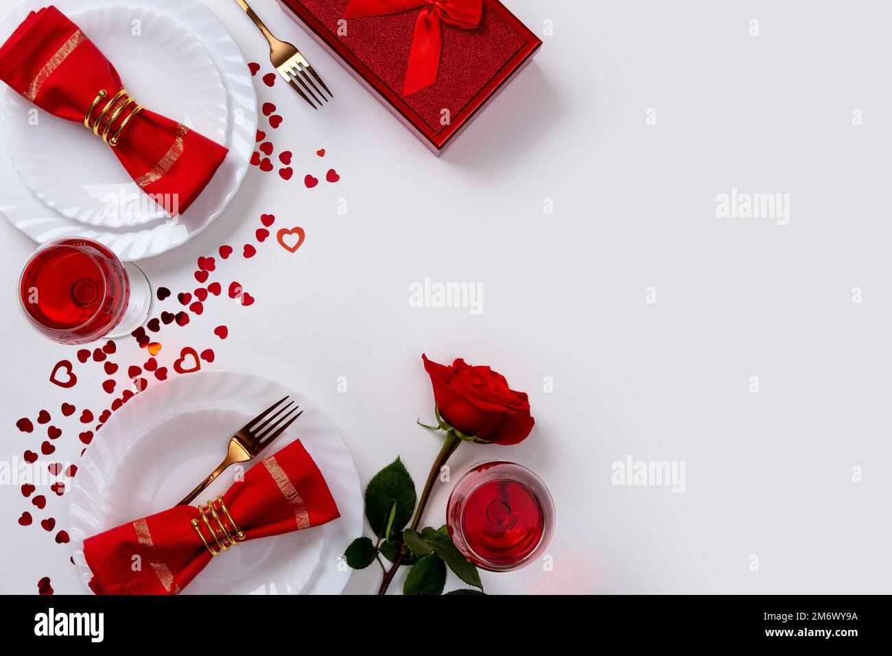 Romantic table setting with white dinnerware and red napkins, wine and candles. Valentines day ...