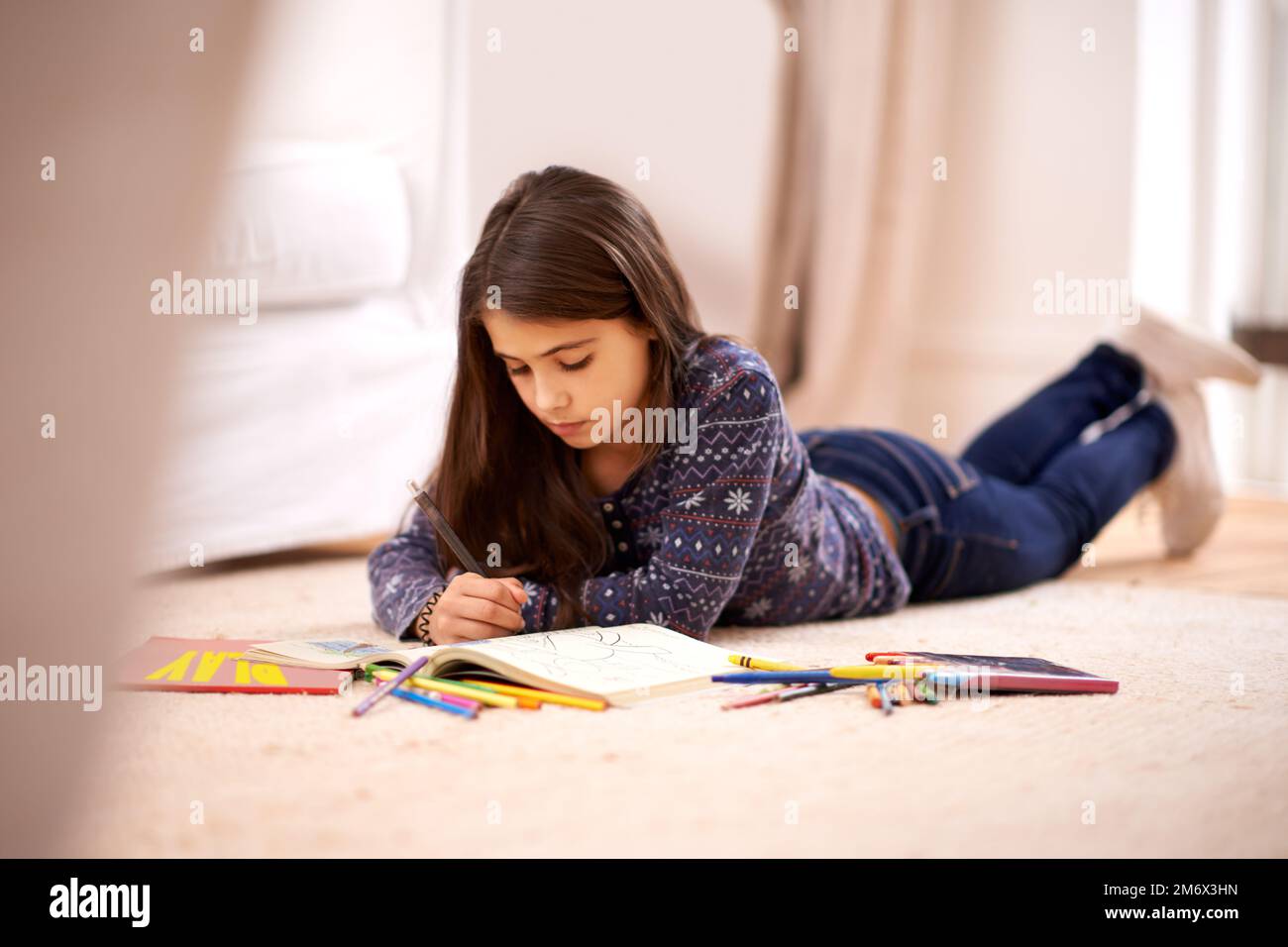 Adding color to her life. A young girl coloring while lying on the ...