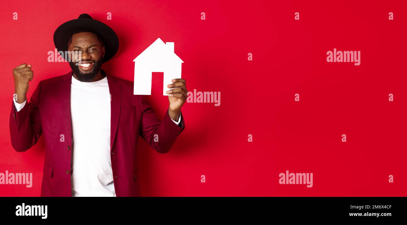 Real estate. Cheerful Black man rejoicing and showing paper home maket ...