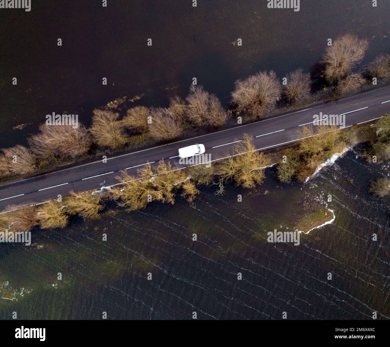 A van drives on. road surrounded by floodwater as the Welney wash fills ...