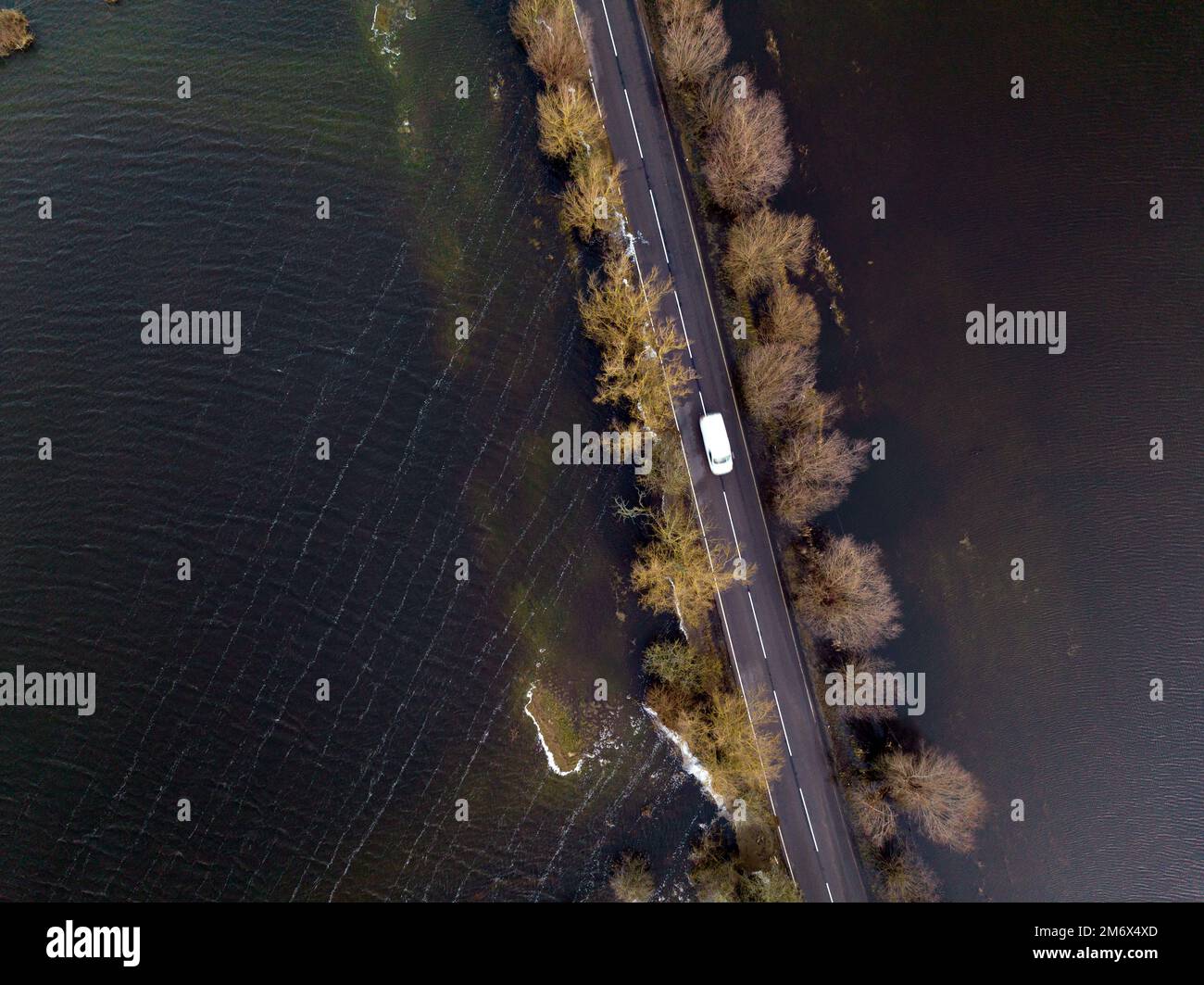A van drives on. road surrounded by floodwater as the Welney wash fills ...