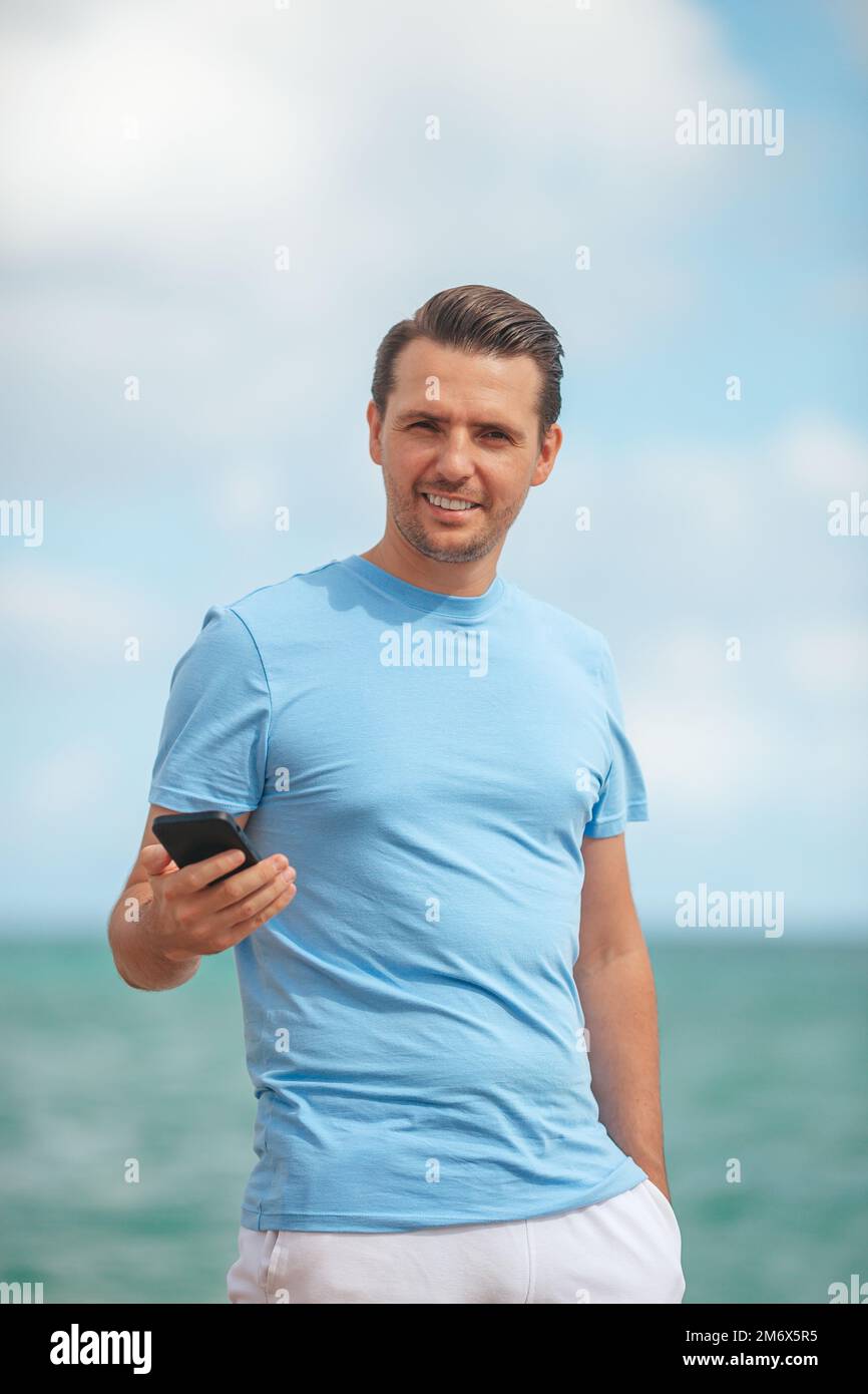 Young man holding mobile phone in his hand while walking on the beach ...