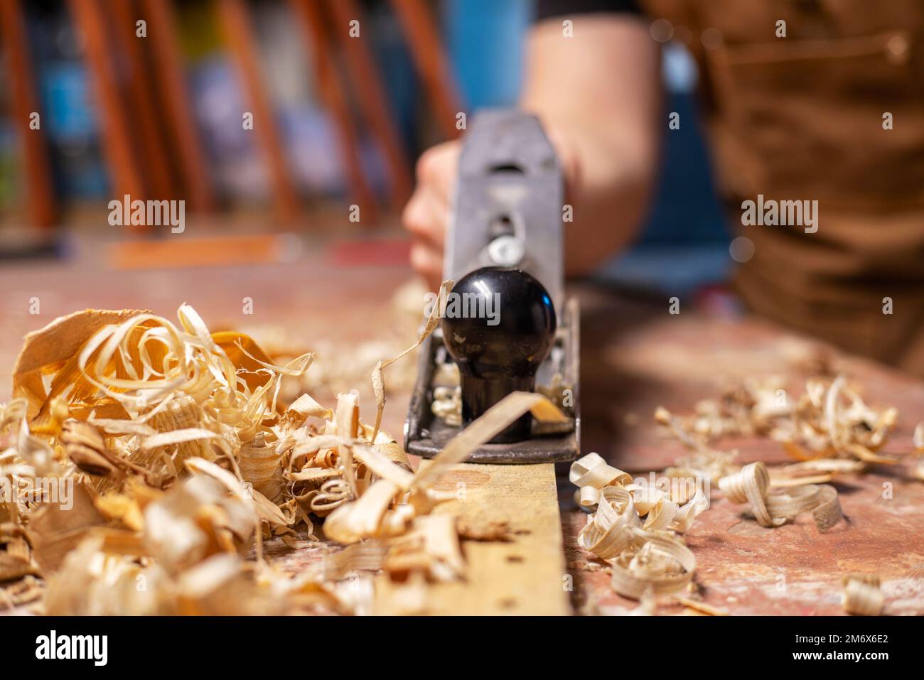 Carpenter in an apron planing a wooden board with a planer, workplace ...