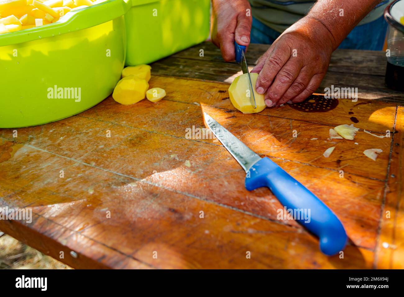 An elderly farmer cooker cuts potatoes using knife into slices on the ...