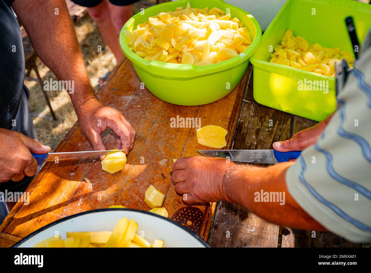 Teamwork of two farmer cookers cut potatoes using knives into slices on ...