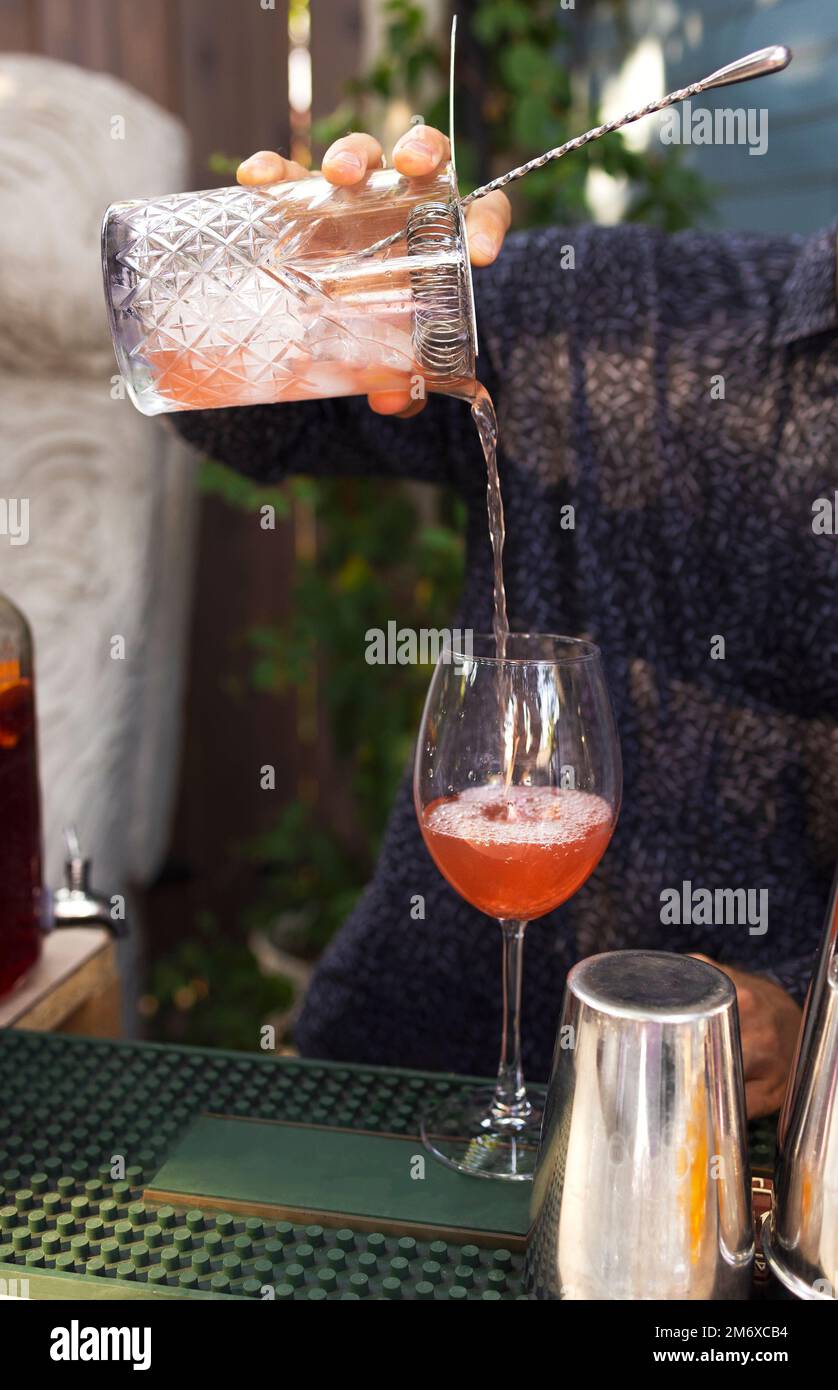 Glasses of cocktails on the bar. Bartender pours a glass of sparkling wine with red alcohol ...