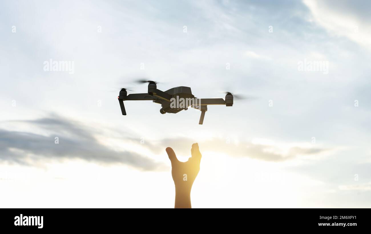 Hand reaching for drone outdoors at sunrise. Testing an aerial unmanned ...