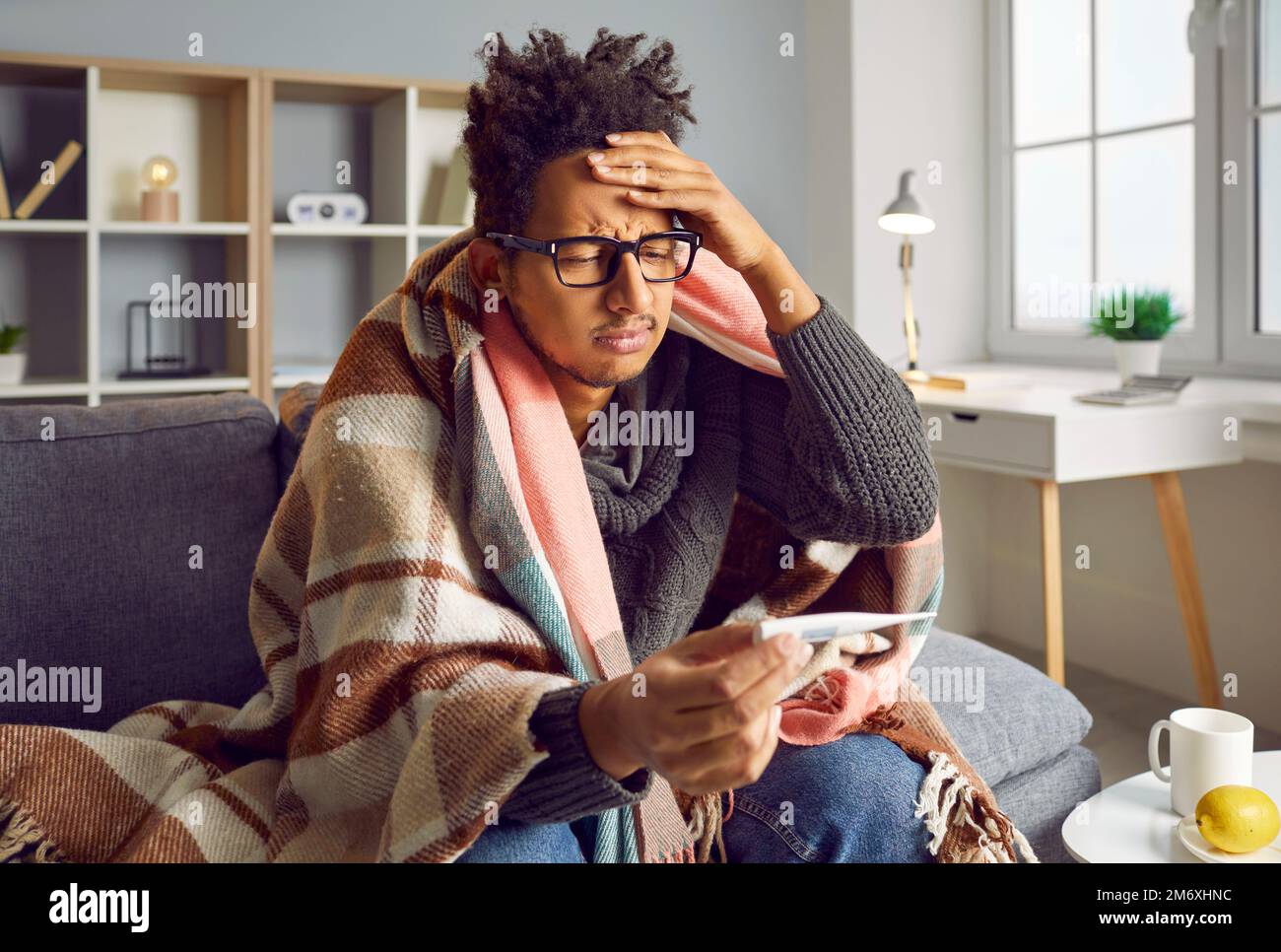 Young African American man has a fever, measures his temperature and ...