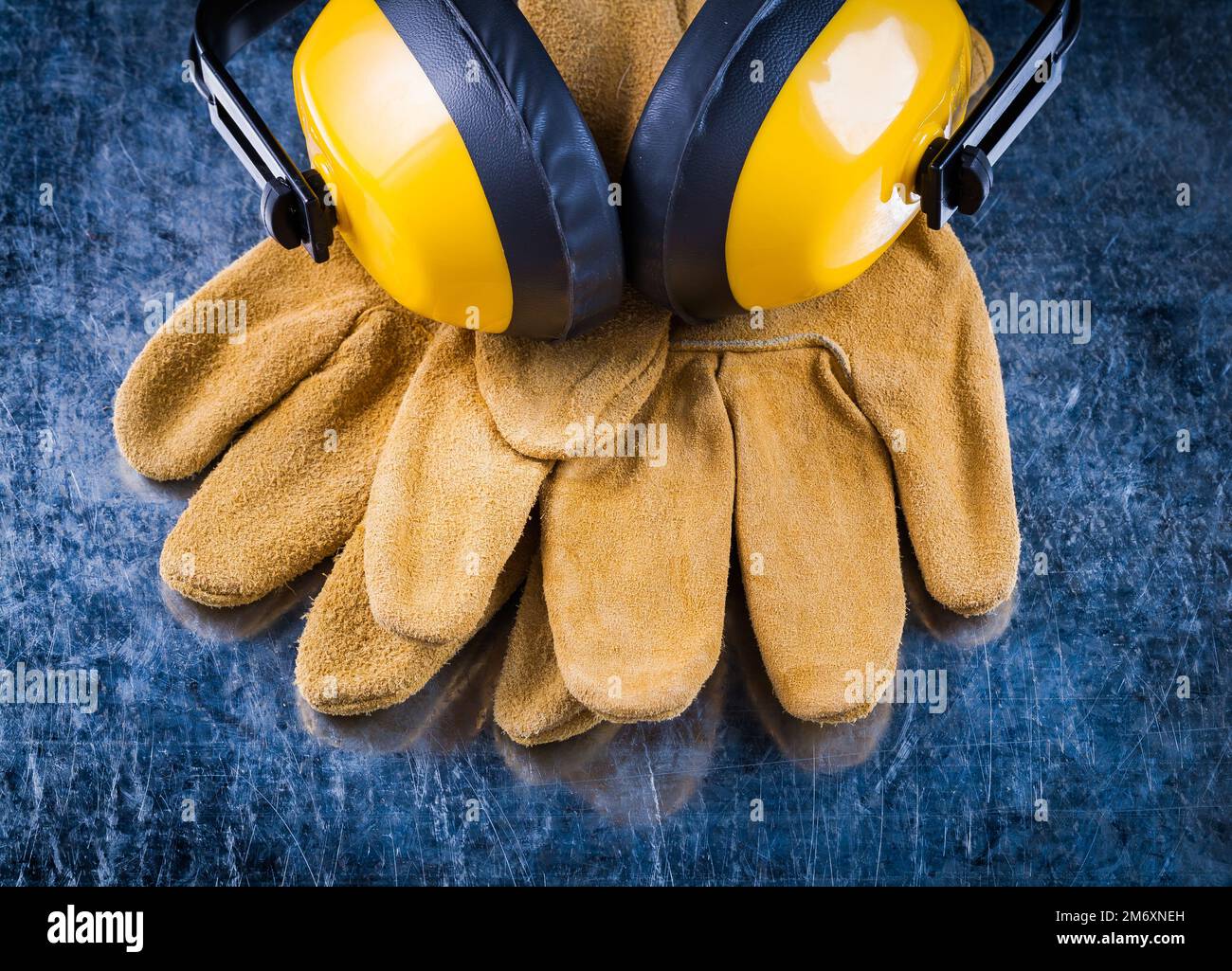 Leather safety gloves and noise insulation ear muffs on scratched ...