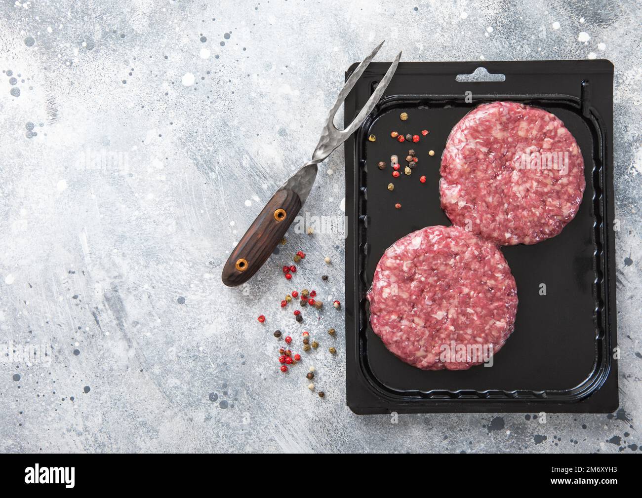 Beef fresh raw burgers in vacuum tray with fork and pepper on light ...