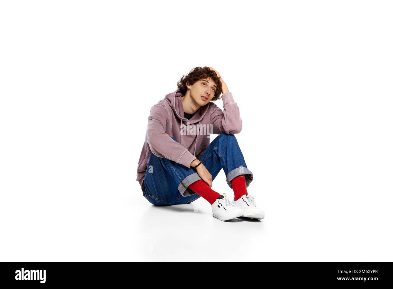 Portrait of young boy sitting over white background. Feeling sad ...