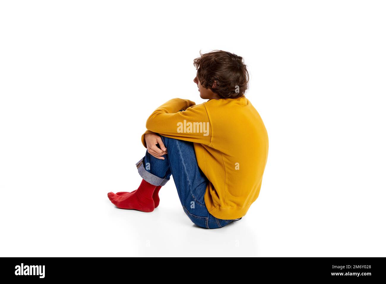 Portrait of young boy sitting on floor in depression, hugging legs over white background ...