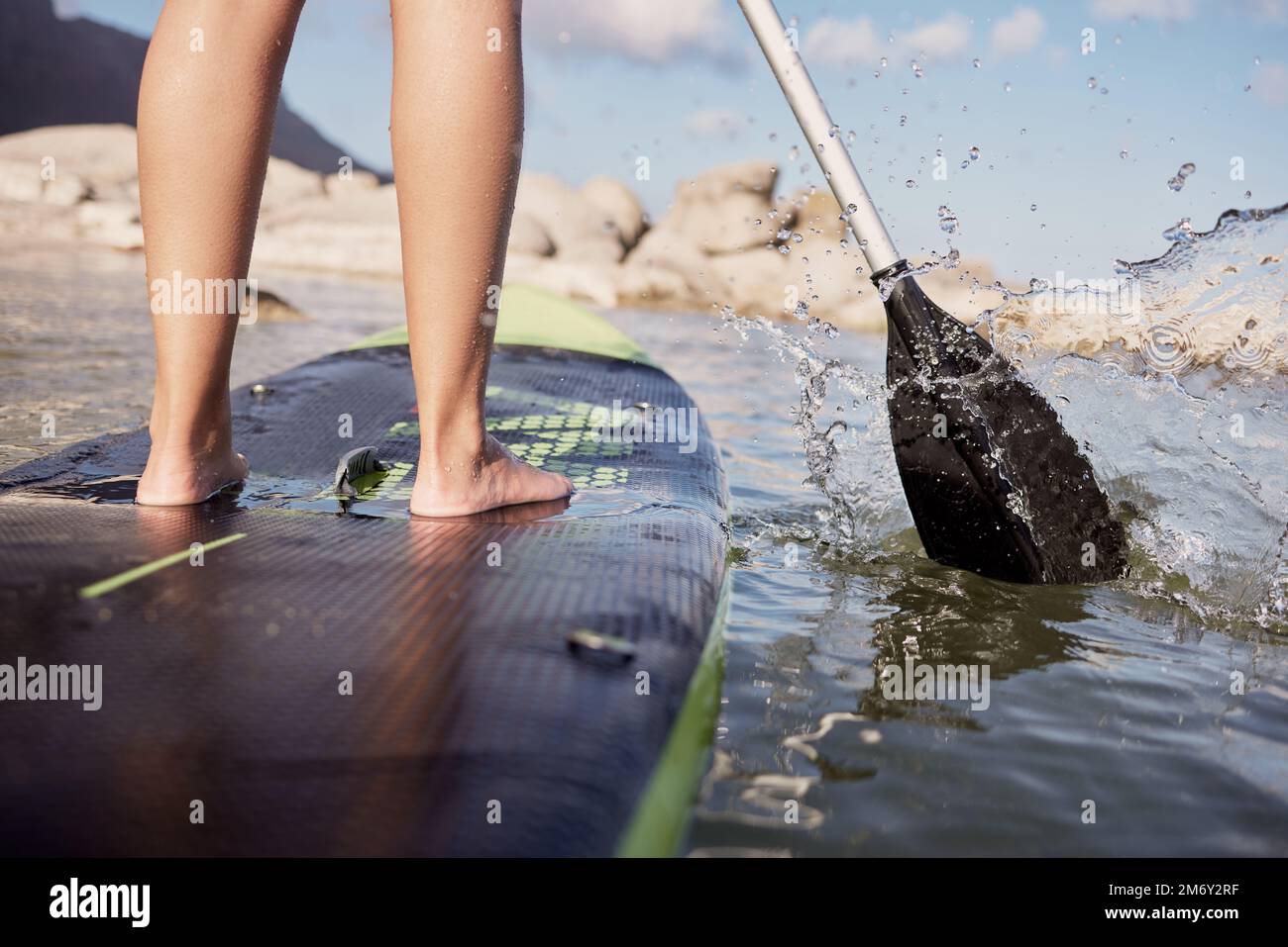 Feet, paddle surf and water with a sports woman standing on a paddle ...