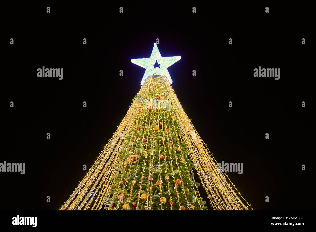 Christmas tree with yellow garlands, decorative bulbs and big white ...