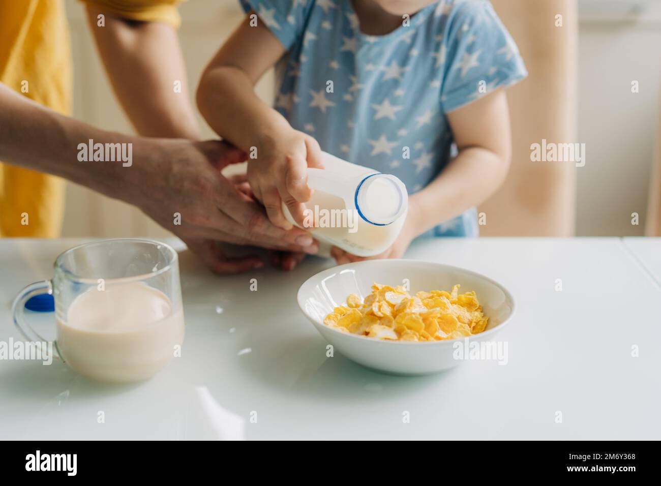 Close-up unrecognizable child and mother preparing corn flakes with ...