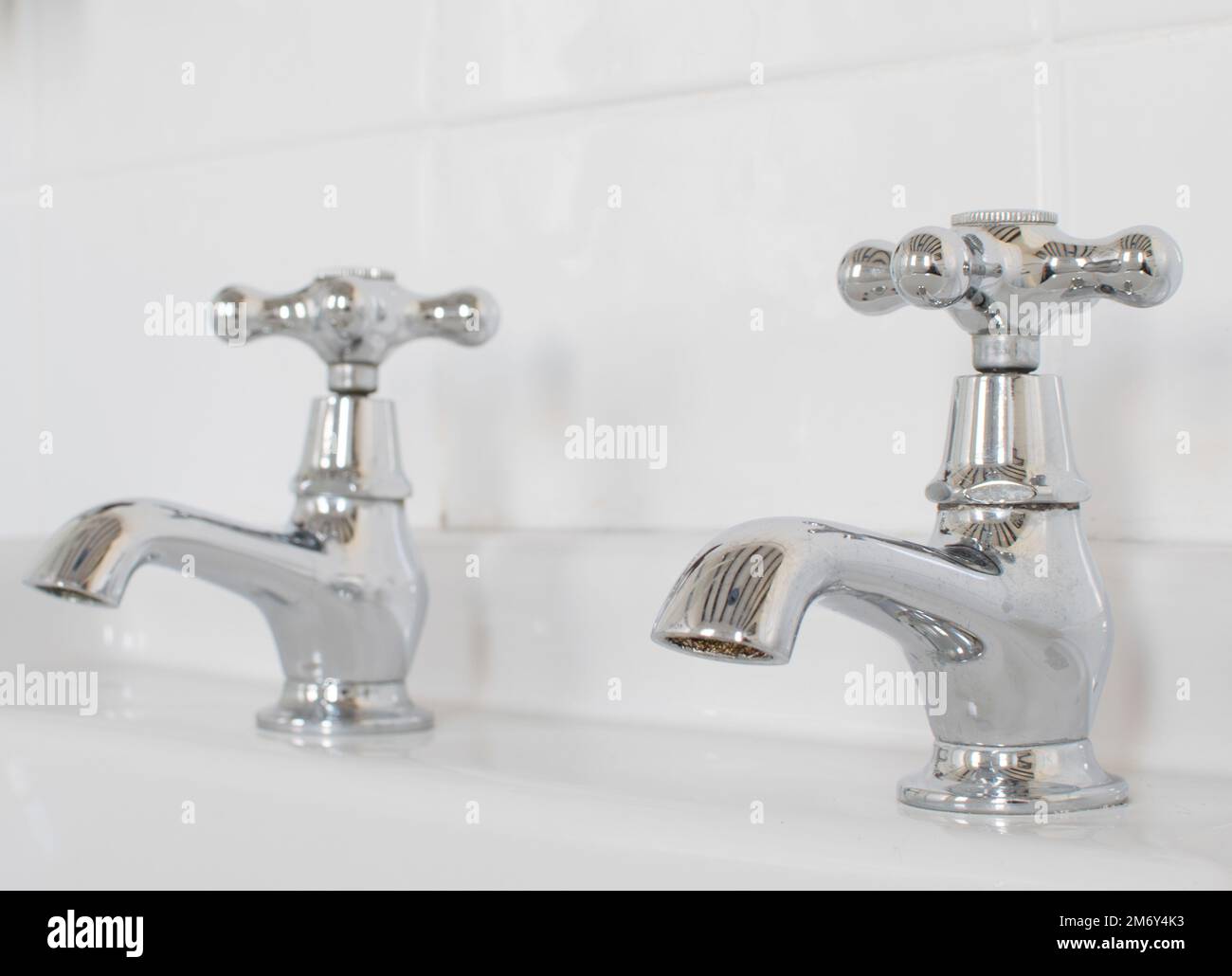 Vintage chrome taps on sink, white tiled background in bathroom, close ...