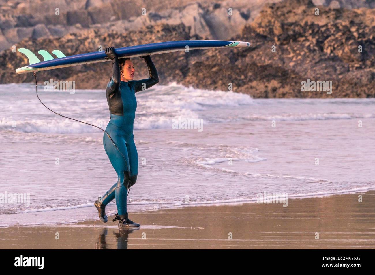 A tired surfer carrying her surfboard on her head and walking out of ...